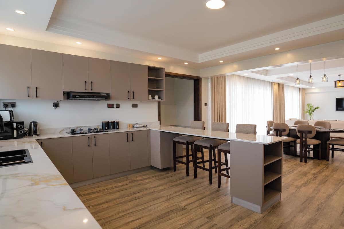 Cozinha moderna com ilha central, área de jantar com televisão e sala de estar com sofá e planta.