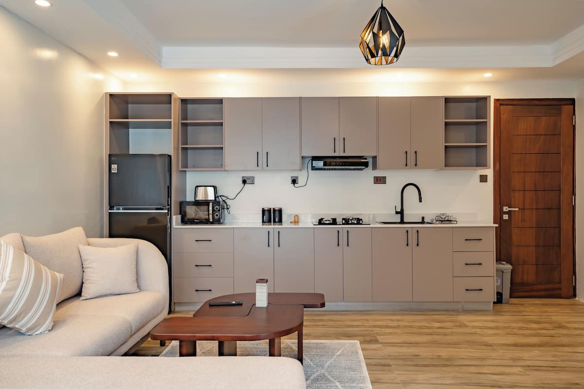 Uma cozinha moderna com eletrodomésticos embutidos, um espaço de refeições com sofá e mesa de centro, e uma porta de madeira.