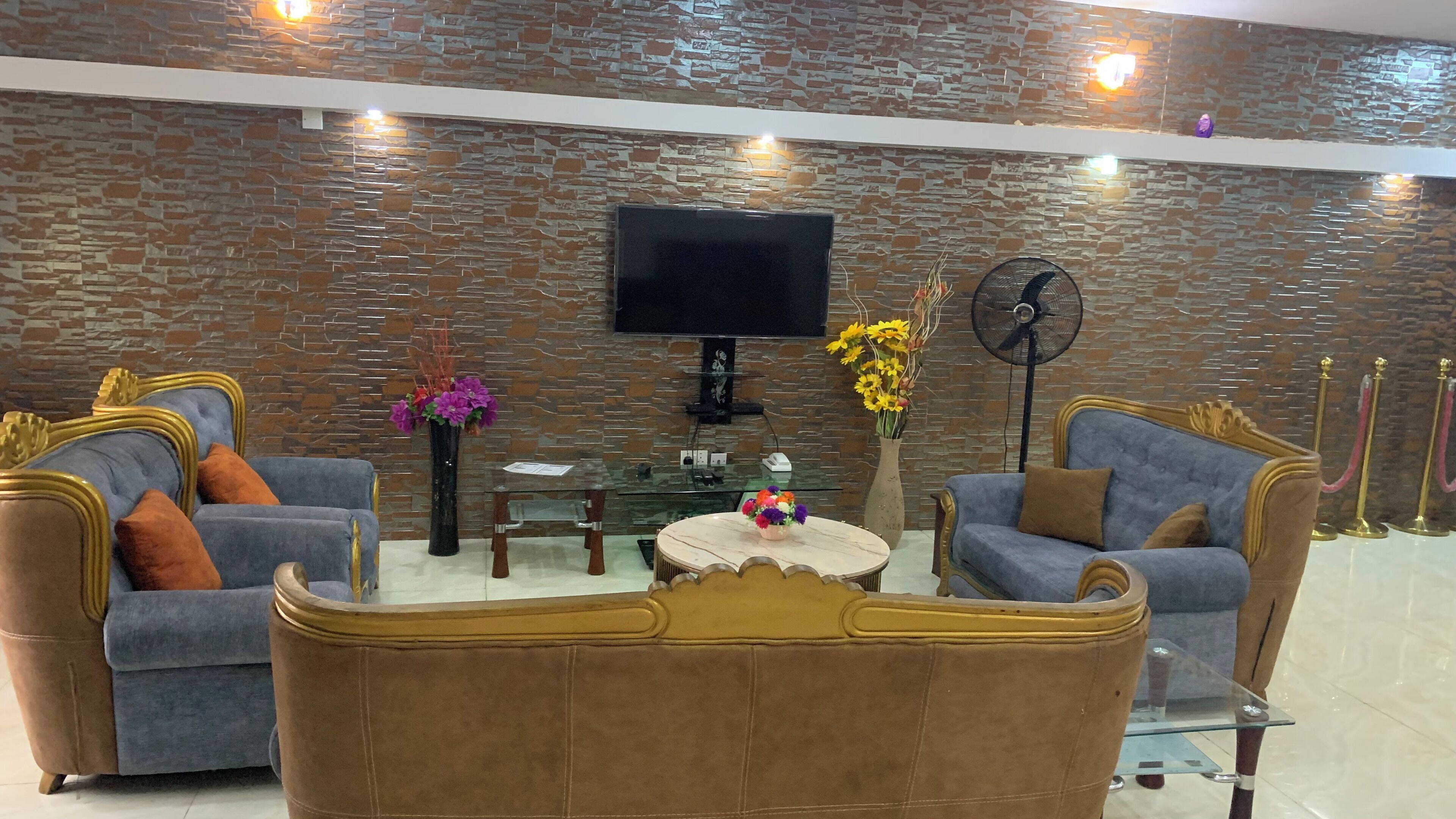Uma sala de estar moderna com parede de tijolos, uma TV de tela plana, dois sofás, uma mesa de centro e um ventilador.
