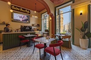 Um café com balcão, cadeiras e mesas vermelhas. Há uma grande janela com vista para prédios.