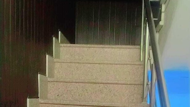 Degraus de pedra com corrimãos de metal que levam a um espaço interior escuro.