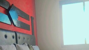 Quarto de hotel com duas camas, uma parede de destaque vermelha e uma janela grande.