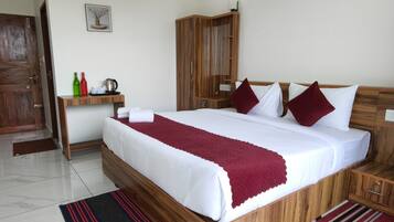 Quarto de hotel com uma cama grande, cabeceira de madeira, mesa de cabeceira com chaleira e criado-mudo.