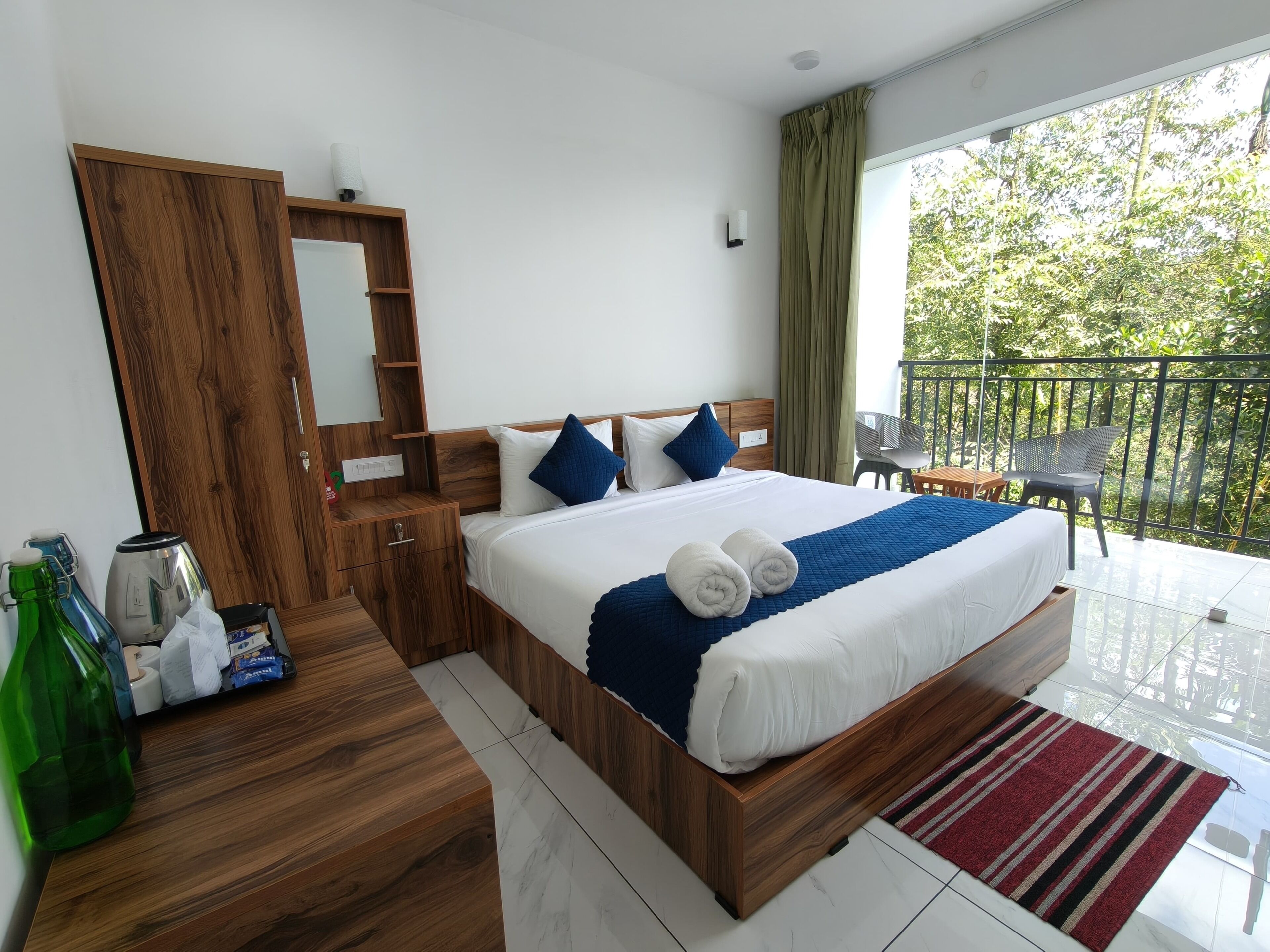 Quarto de hotel moderno com cama de madeira, varanda com vista para áreas verdes e um pequeno espaço de estar.