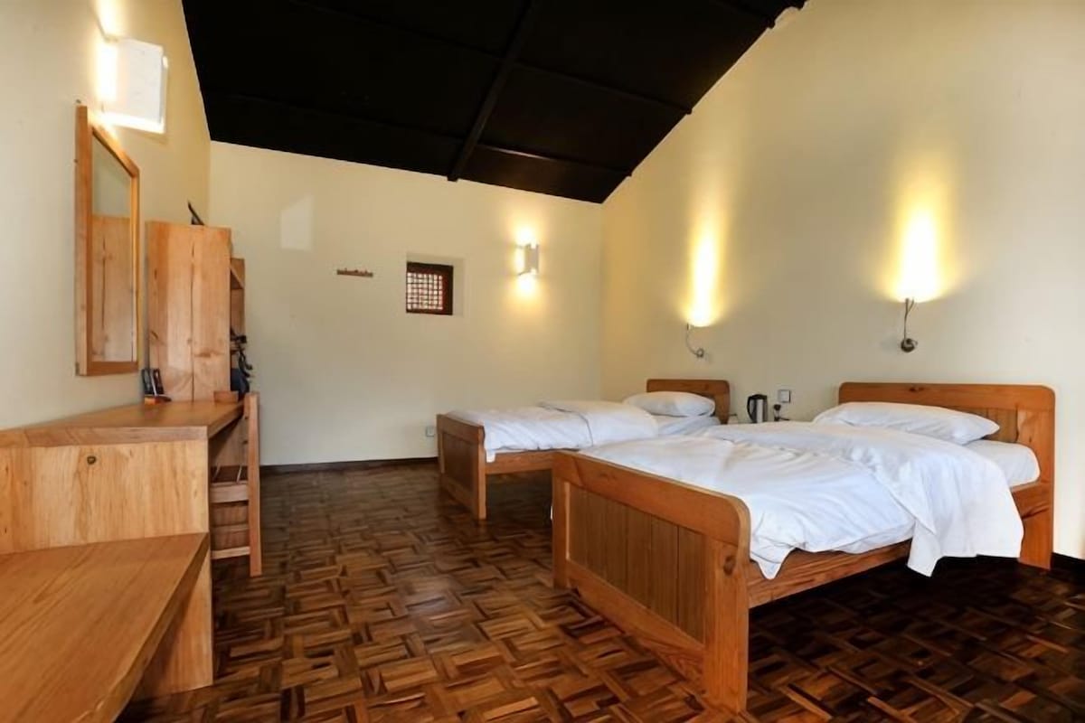 Quarto com duas camas de madeira, uma escrivaninha de madeira e um banco.