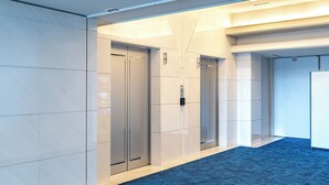 Área de elevador moderna com carpete azul e parede revestida de azulejos brancos.