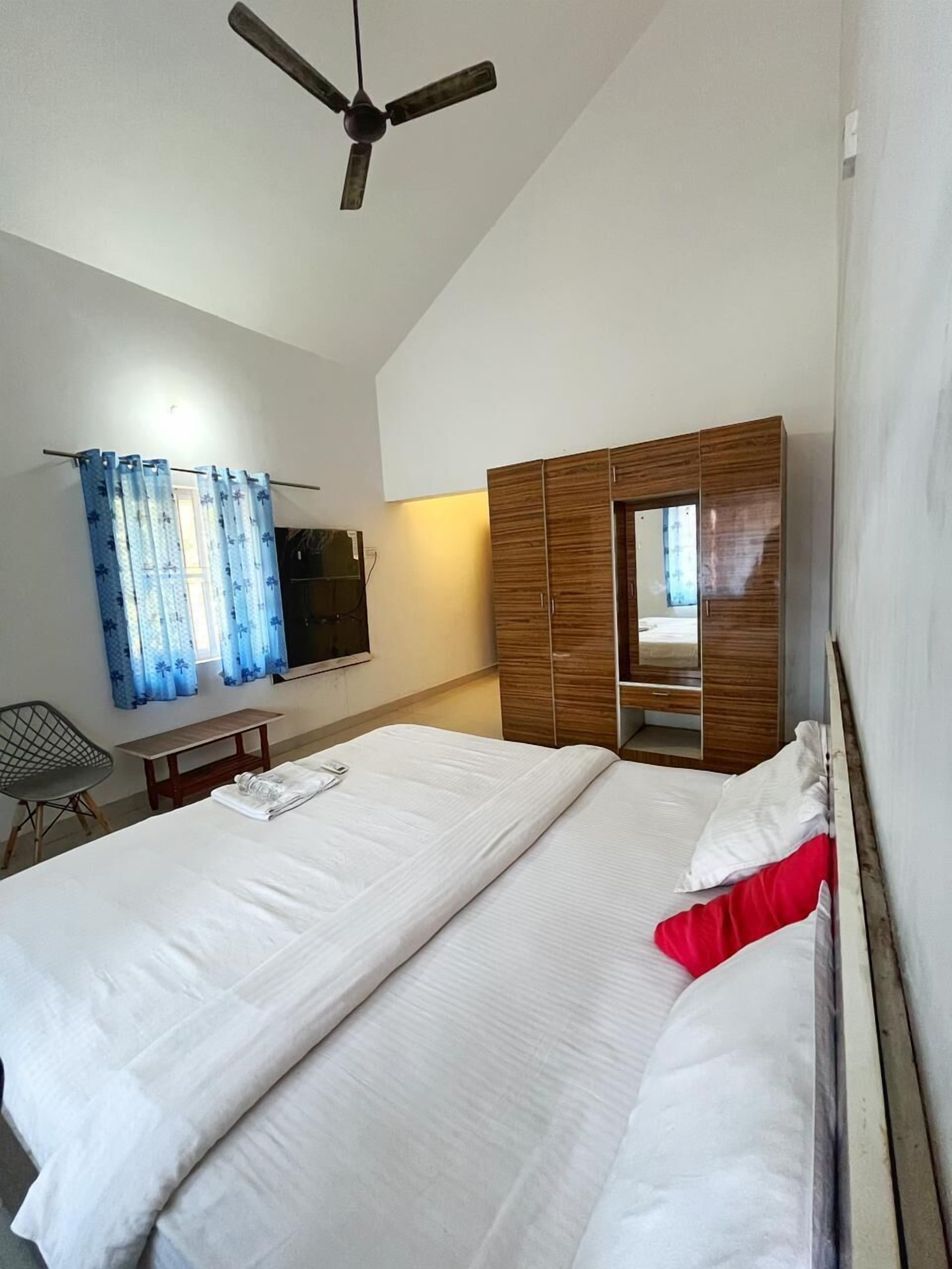 Quarto com cama, guarda-roupa de madeira, ventoinha no teto, televisão e uma cadeira.