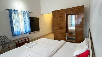 Quarto com cama, guarda-roupa de madeira, ventoinha no teto, televisão e uma cadeira.