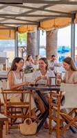 Um grupo de pessoas sentadas em uma mesa ao ar livre, com vista para o mar.