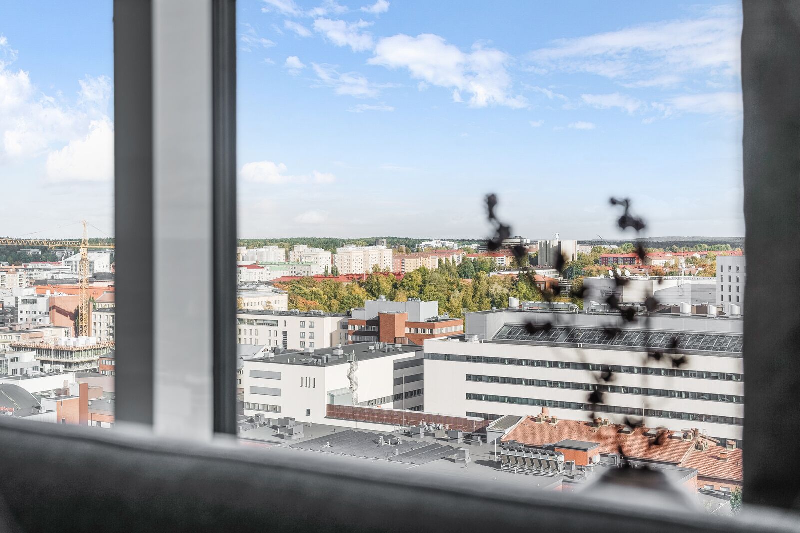 Vista da janela com uma paisagem urbana, edifícios, árvores e céu claro.
