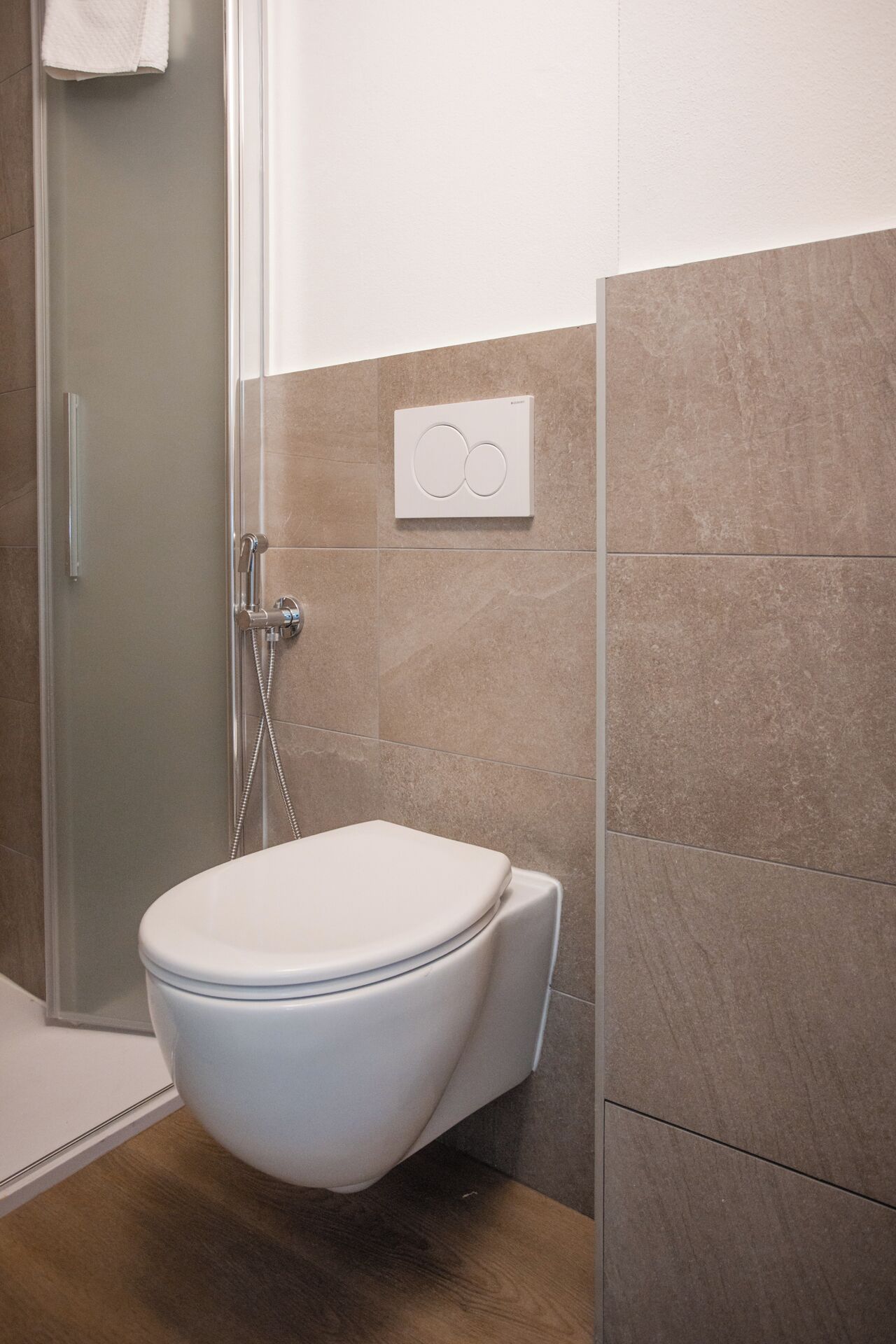 Uma casa de banho moderna com sanita branca, cabine de duche em vidro e painel de controlo fixado na parede.
