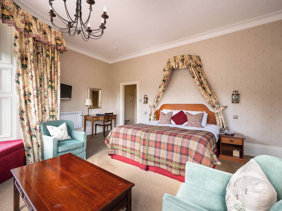 Um quarto com uma cama grande, uma mesa de cabeceira de madeira, uma escrivaninha, uma cadeira e um banco vermelho.