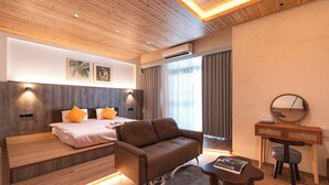 Quarto de hotel moderno com teto de madeira, cama com almofadas laranja, sofá marrom, mesinha com uma revista e espelho sobre um console de madeira.
