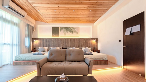 Quarto moderno com teto de madeira, uma cama grande, um sofá e uma mesa de cabeceira com abajur.