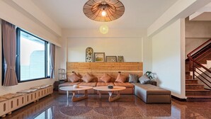Sala de estar moderna com parede de madeira, um sofá, dois mesinhos e uma escada à direita.