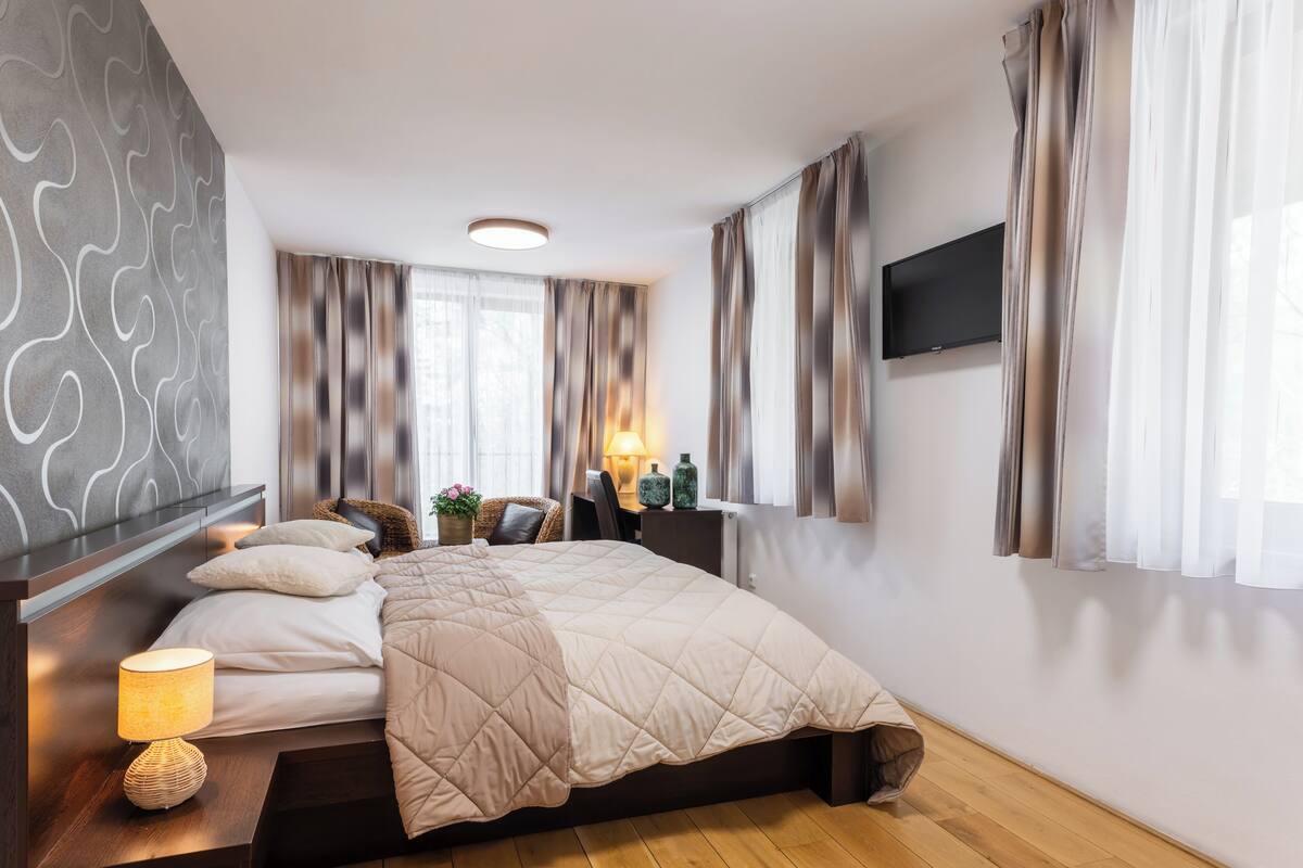 Quarto de hotel moderno com uma cama grande, televisão de tela plana, luminária e vista para o exterior.