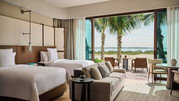 Quarto de hotel com duas camas, um sofá, uma mesa de jantar e vista para a praia.