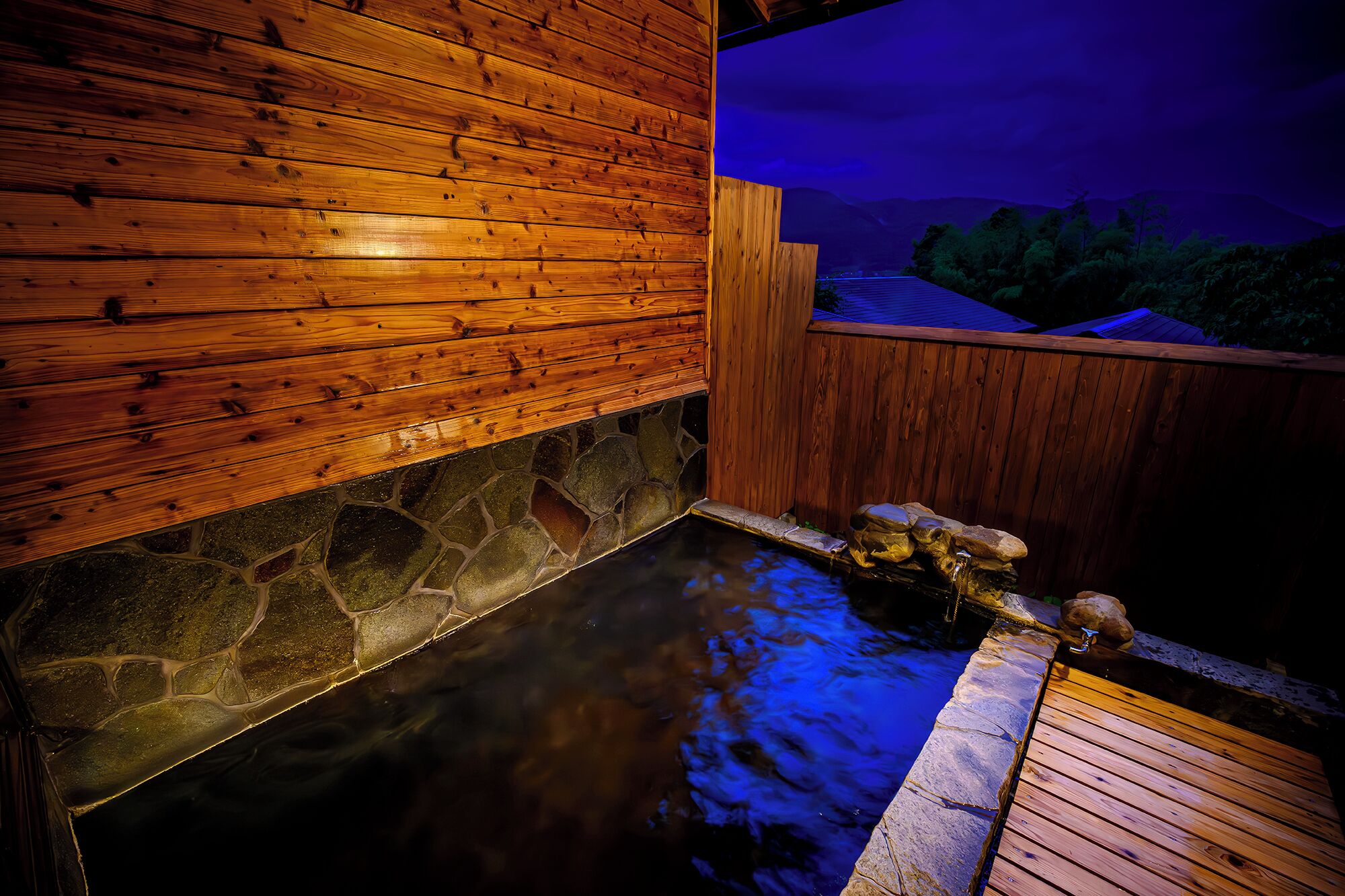 Um spa de madeira com parede de pedra, deck de madeira e vista para montanhas.