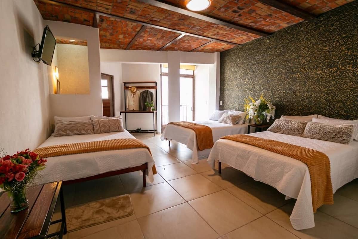 Quarto de hotel com duas camas, teto de tijolos, parede decorativa e uma pequena mesa com um vaso de flores.