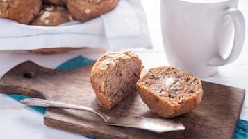 Um pão sobre uma tábua de madeira, uma xícara de café e uma colher.