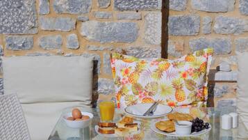 Mesa de café da manhã com ovos, torradas, frutas e suco em frente a uma parede de pedra.