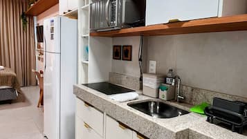 Uma cozinha compacta com micro-ondas embutido, pia e bancada com torradeira.