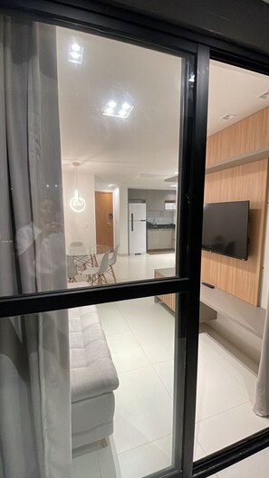 Uma sala de estar moderna com sofá, área de jantar com cadeiras, cozinha com geladeira e televisão na parede.