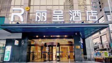 Entrada de hotel com fachada de vidro, um logotipo 'R' em destaque e uma placa com caracteres chineses.