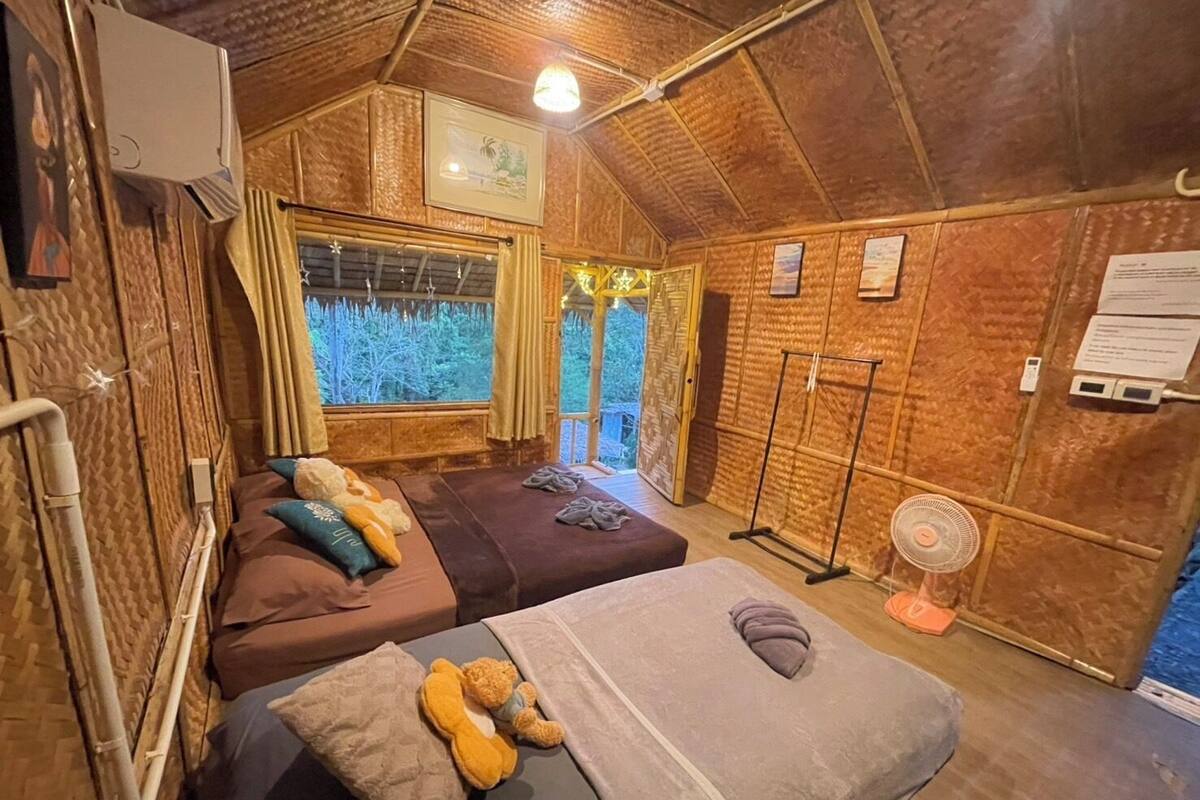 Quarto aconchegante com duas camas, um ventilador e uma janela com cortinas.
