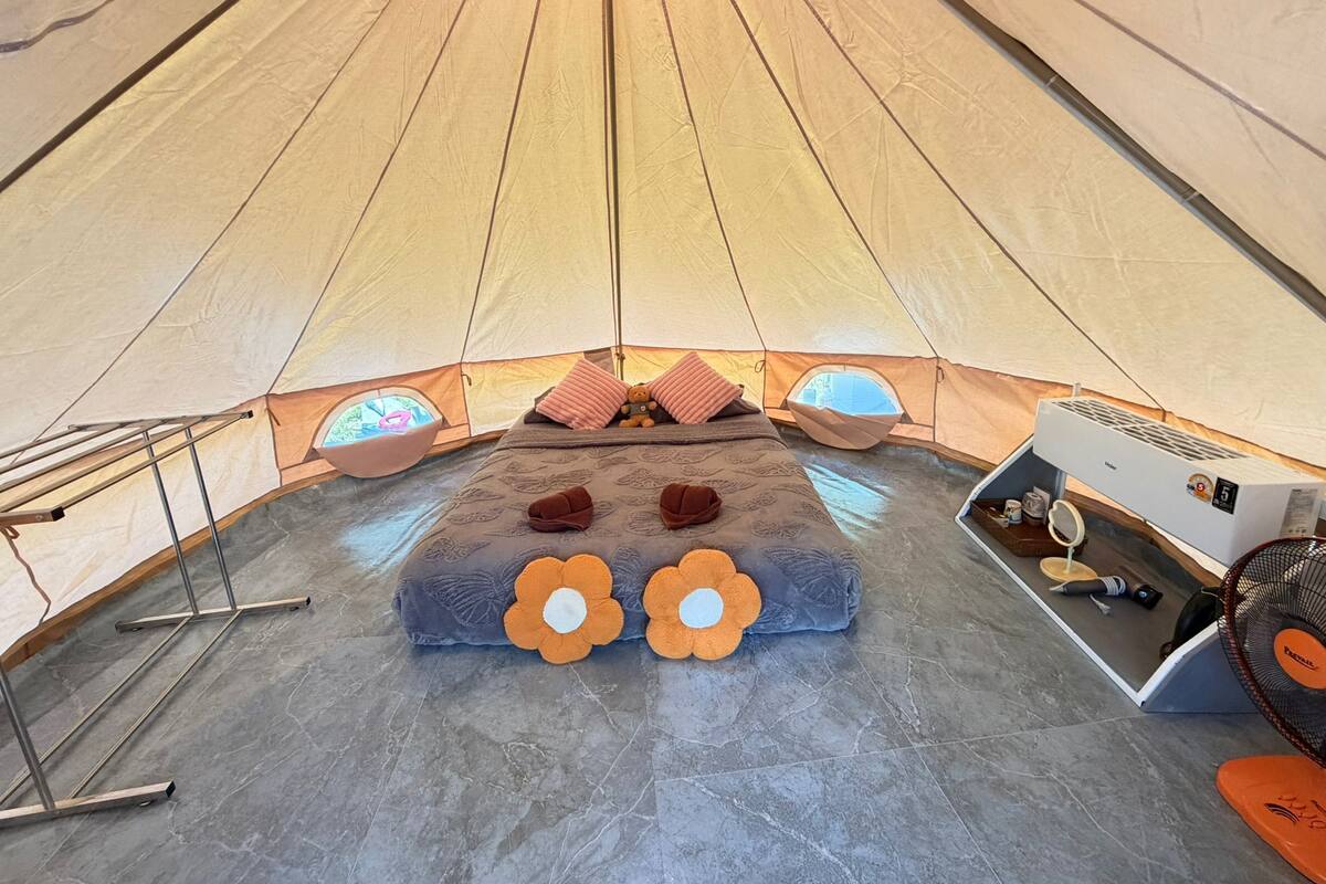 Uma tenda com cama, almofadas, um ventilador e uma janela.