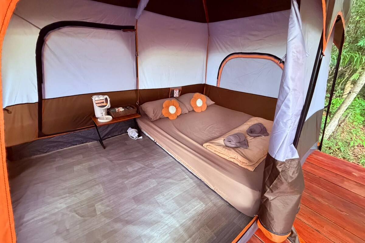 Uma tenda com uma cama, uma mesinha com uma chaleira e uma tomada.