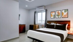 Quarto de hotel com cama, mesa de cabeceira, janela e obras de arte na parede.