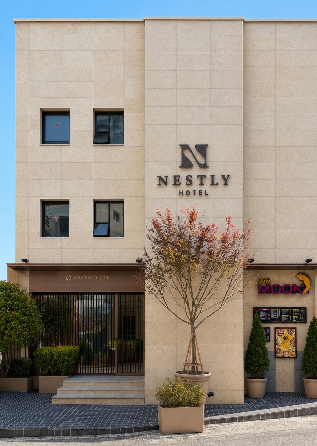Edifício do Nestly Hotel com fachada moderna, um letreiro Cafe Moon e uma árvore em primeiro plano.