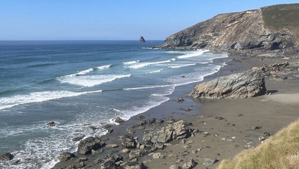 Paisagem costeira com praia rochosa, ondas e um penhasco.