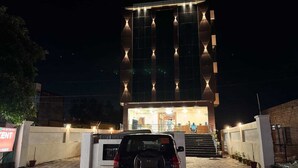 Um edifício moderno com entrada central, uma escadaria que leva à entrada e um carro estacionado na frente.