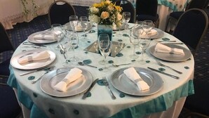 Mesa de jantar redonda posta para seis pessoas, com pratos, talheres e copos.