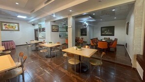Um restaurante espaçoso com diversas áreas de refeição, incluindo uma mesa central rodeada de cadeiras e uma seção separada com uma mesa comprida e cadeiras.
