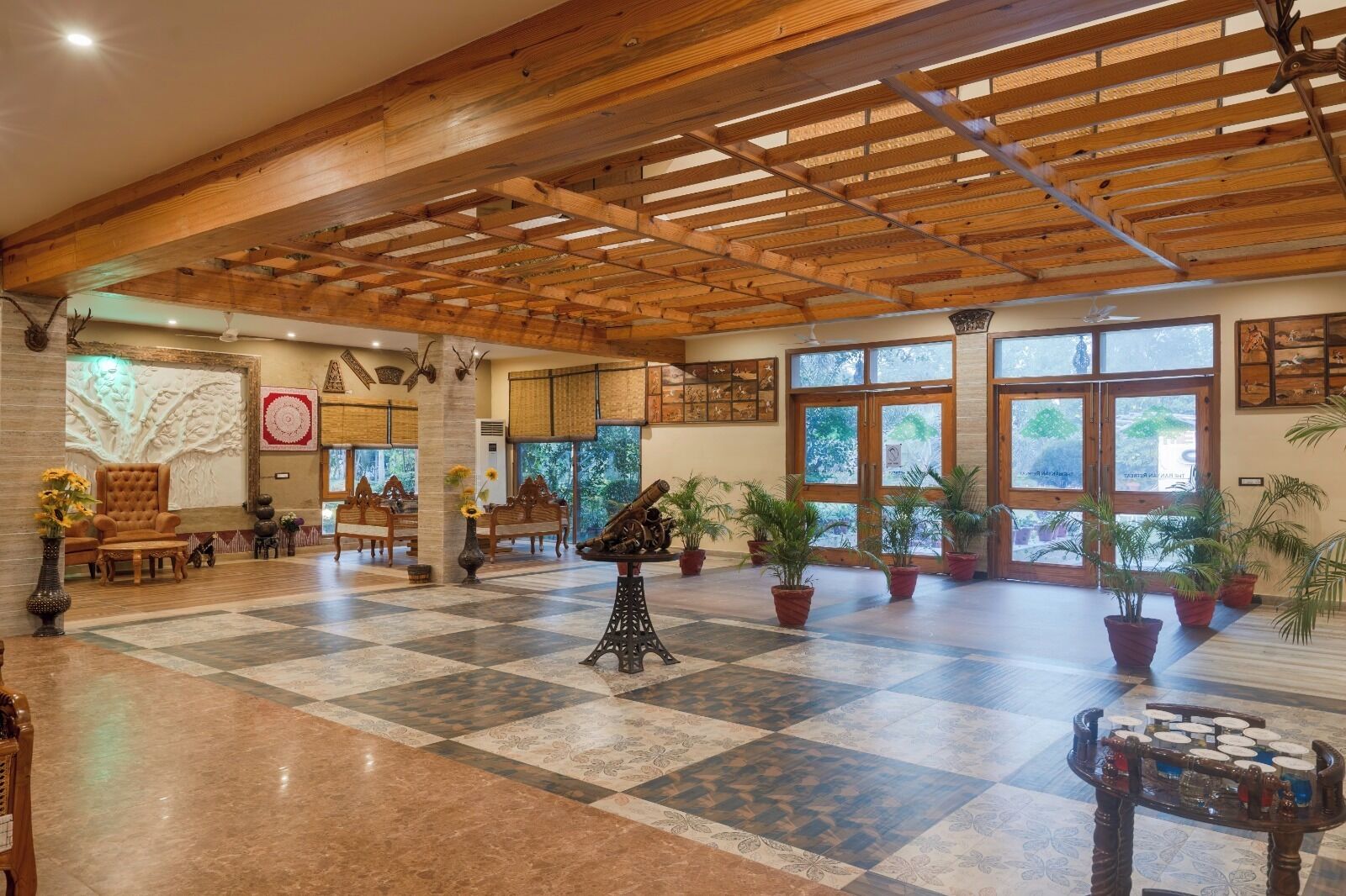 Um hall amplo com teto de madeira alta, pisos de azulejos quadriculados e várias plantas em vasos.