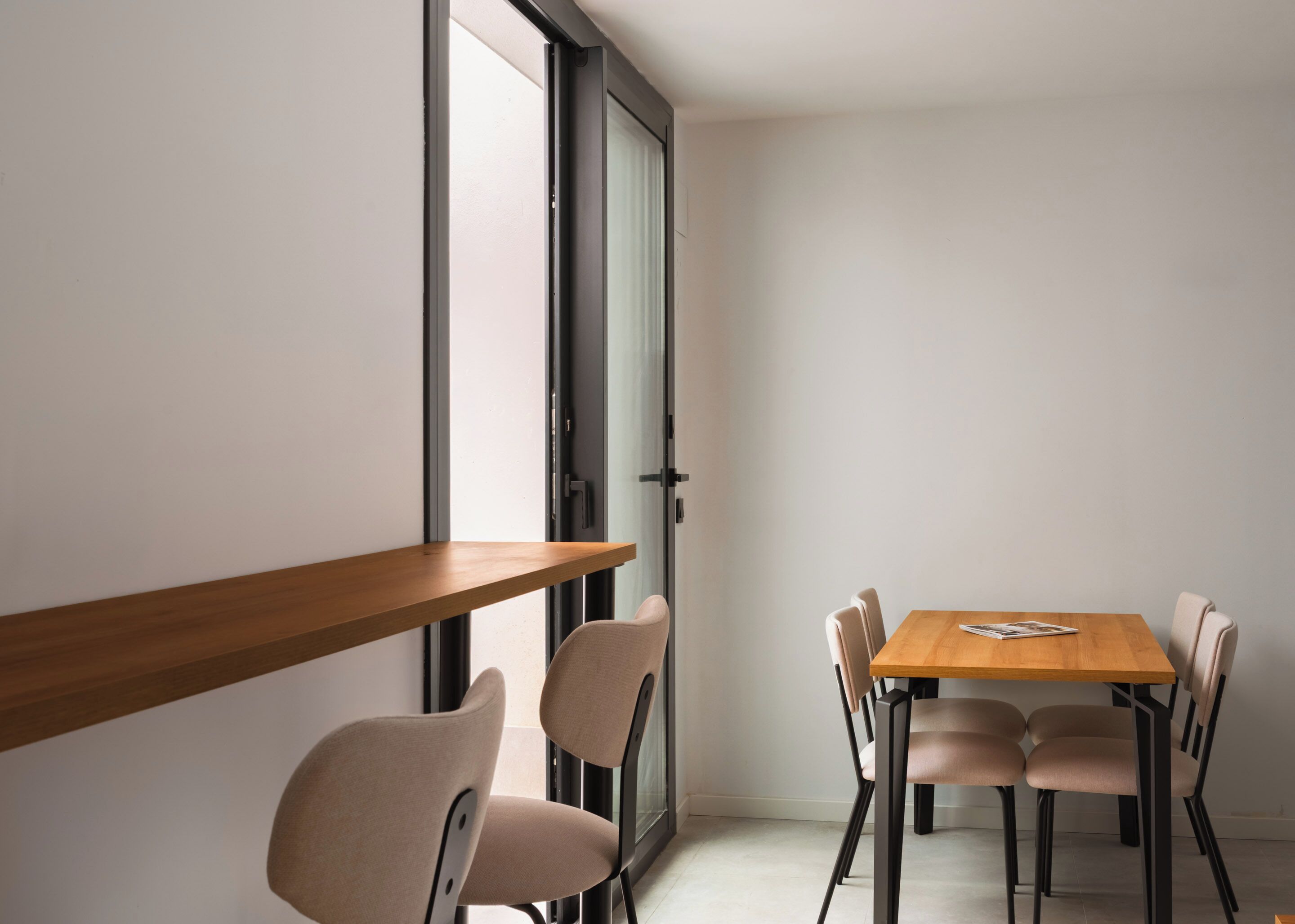 Uma sala de jantar moderna com mesa de madeira e seis cadeiras, uma estante de madeira e uma porta de vidro que dá para uma varanda.