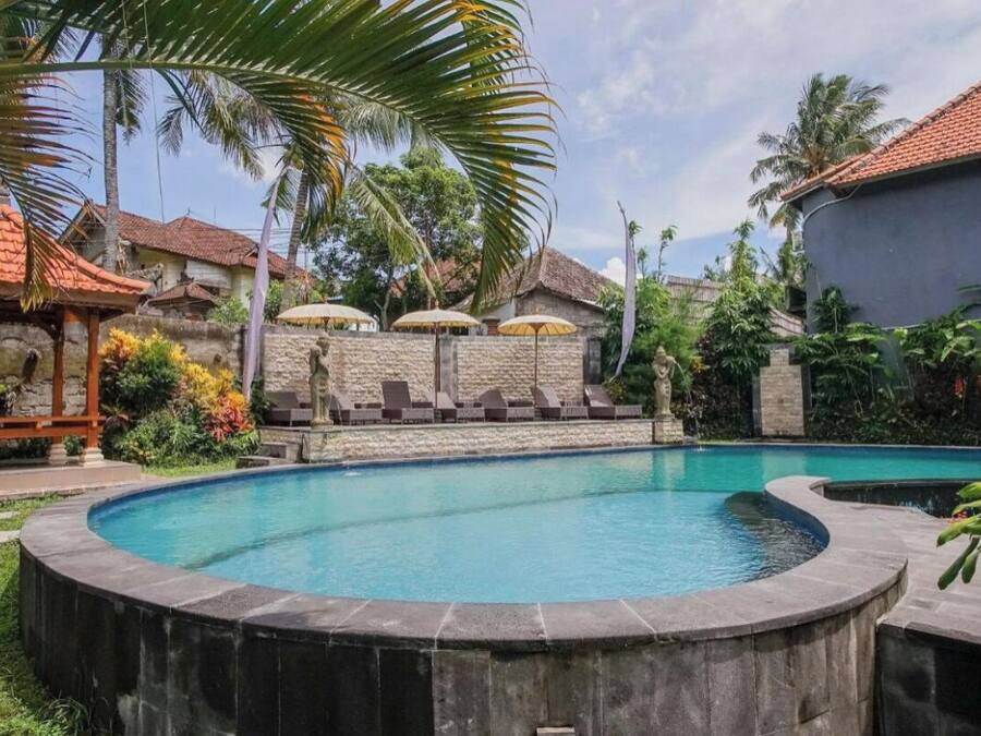 Piscina com espreguiçadeiras e guarda-sóis, cercada por paredes de pedra e plantas tropicais.