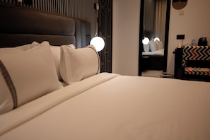 Quarto de hotel com uma cama grande, mesa de cabeceira, espelho e luminária na parede.