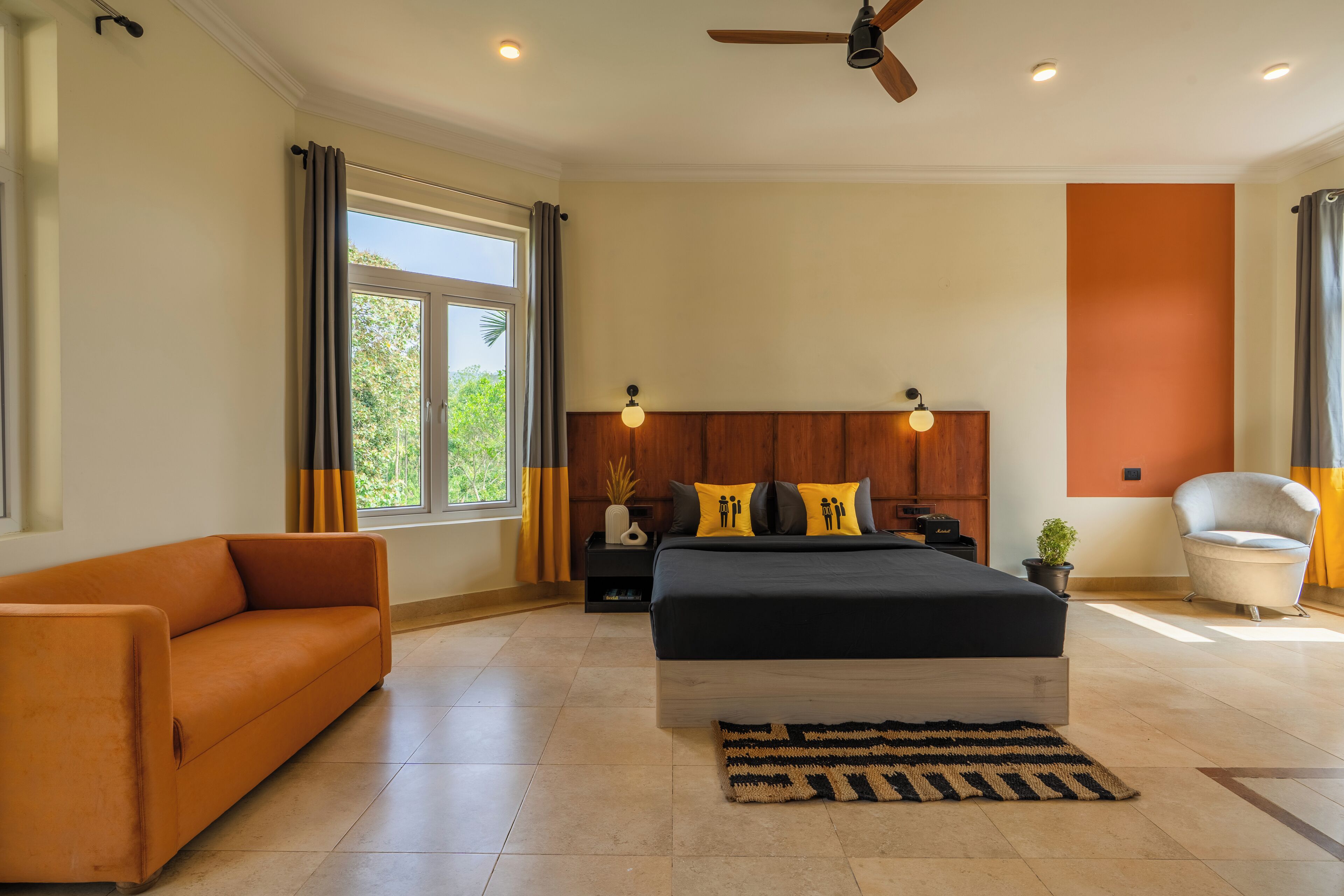 Quarto moderno com uma cama grande, um sofá, ventoinha no teto e vista para o verde lá fora.