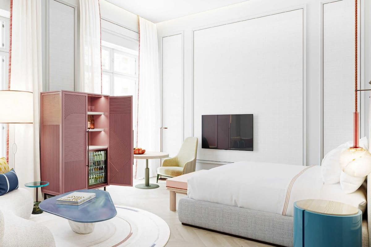 Quarto de hotel moderno com uma cama grande, área de estar com mesa de centro, televisão e minibar.