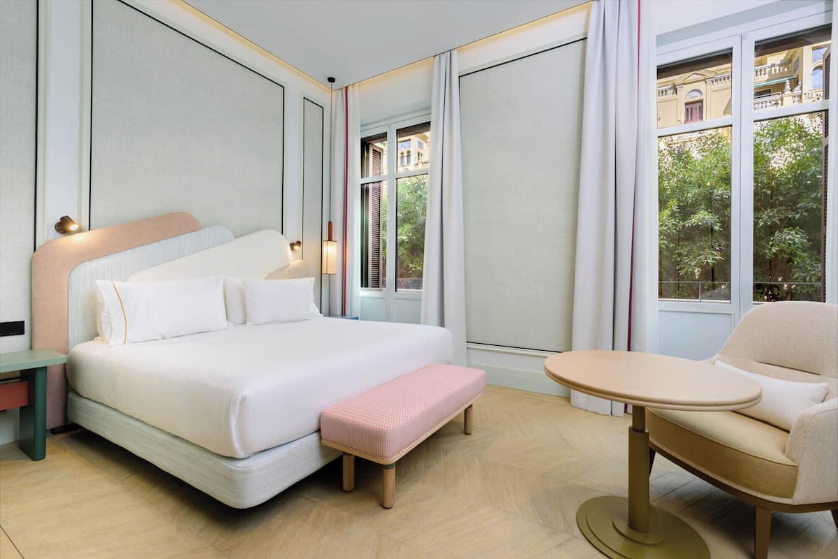 Quarto de hotel com uma cama grande, uma mesa pequena e uma cadeira.