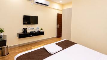 Quarto de hotel com cama, televisão na parede, pequeno móvel com objetos e porta.