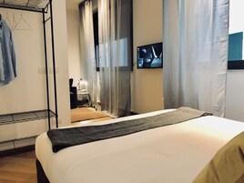 Quarto de hotel com cama, televisão na parede, guarda-roupa e uma pequena mesa com abajur.