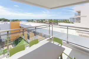 Uma varanda com guarda-corpo de vidro, uma mesa e cadeiras verdes.