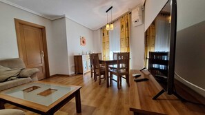 Uma sala de estar com sofá, mesa de centro, mesa de jantar com cadeiras, televisão e uma porta.