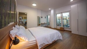 Quarto moderno com uma cama grande, mesa de cabeceira, espelho e vista da cidade por grandes janelas.