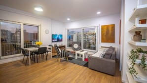 Uma sala de estar moderna com área de jantar, janelas amplas e uma televisão.